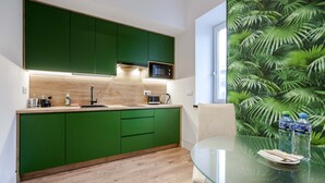Uma cozinha moderna com armários verdes, micro-ondas e uma mesa de vidro com uma cadeira.