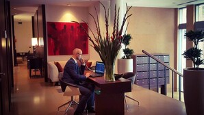 Um hall de hotel moderno, com uma mesa de recepção, uma grande pintura abstrata e uma escada que dá para uma área de armazenamento.