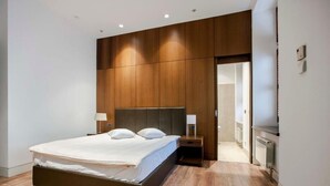 Quarto moderno com uma cama grande, painéis de madeira nas paredes, uma mesa de cabeceira com abajur e um radiador.