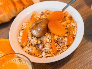 Uma tigela de granola com frutas secas e nozes, acompanhada de um croissant e um copo de suco de laranja.