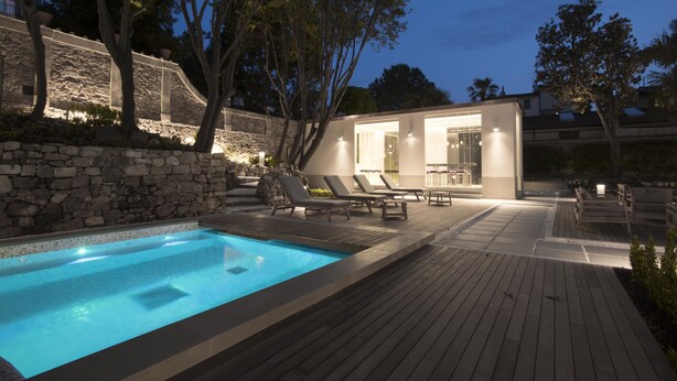 Uma área de piscina moderna ao ar livre, com muro de pedra, deck de madeira e espreguiçadeiras.