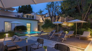 Um pátio moderno ao ar livre com piscina, espreguiçadeiras e guarda-sóis.