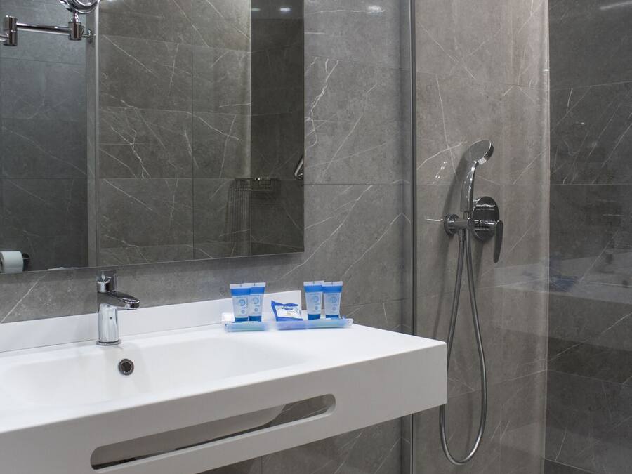 Um banheiro moderno com pia branca, espelho, chuveiro manual e porta-toalhas.