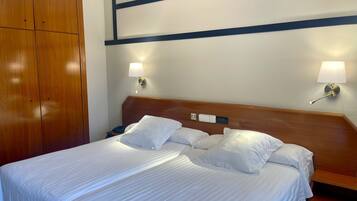 Quarto de hotel com uma cama grande, duas luminárias de cabeceira, um guarda-roupa de madeira e uma parede com design geométrico.