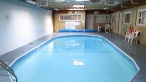 Piscina interior com superfície de água azul, bloco de partida e placa de 'STOP' no teto.