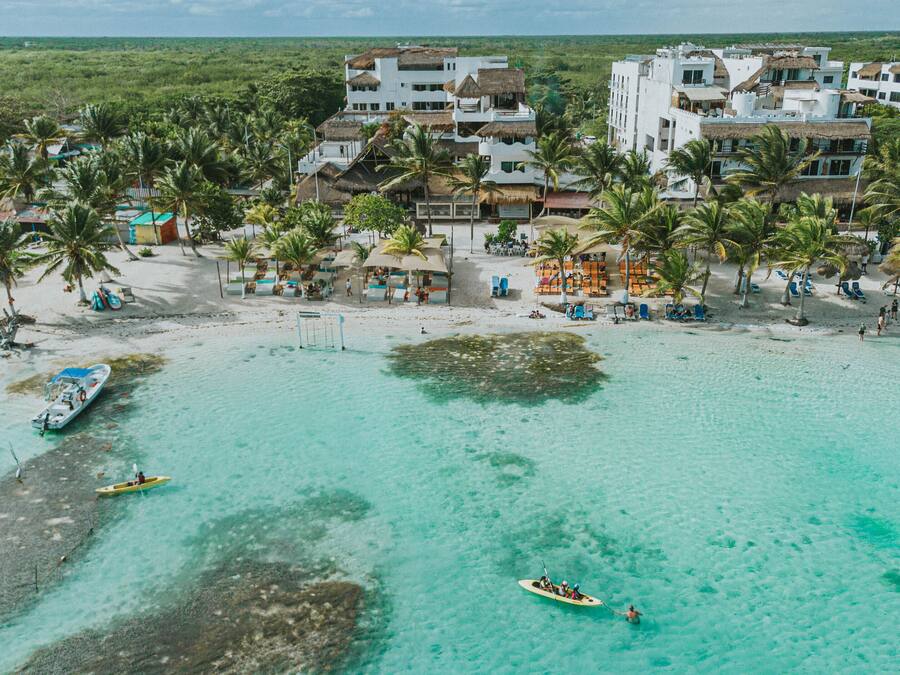 Um resort costeiro com vários edifícios, palmeiras e águas turquesa cristalinas.