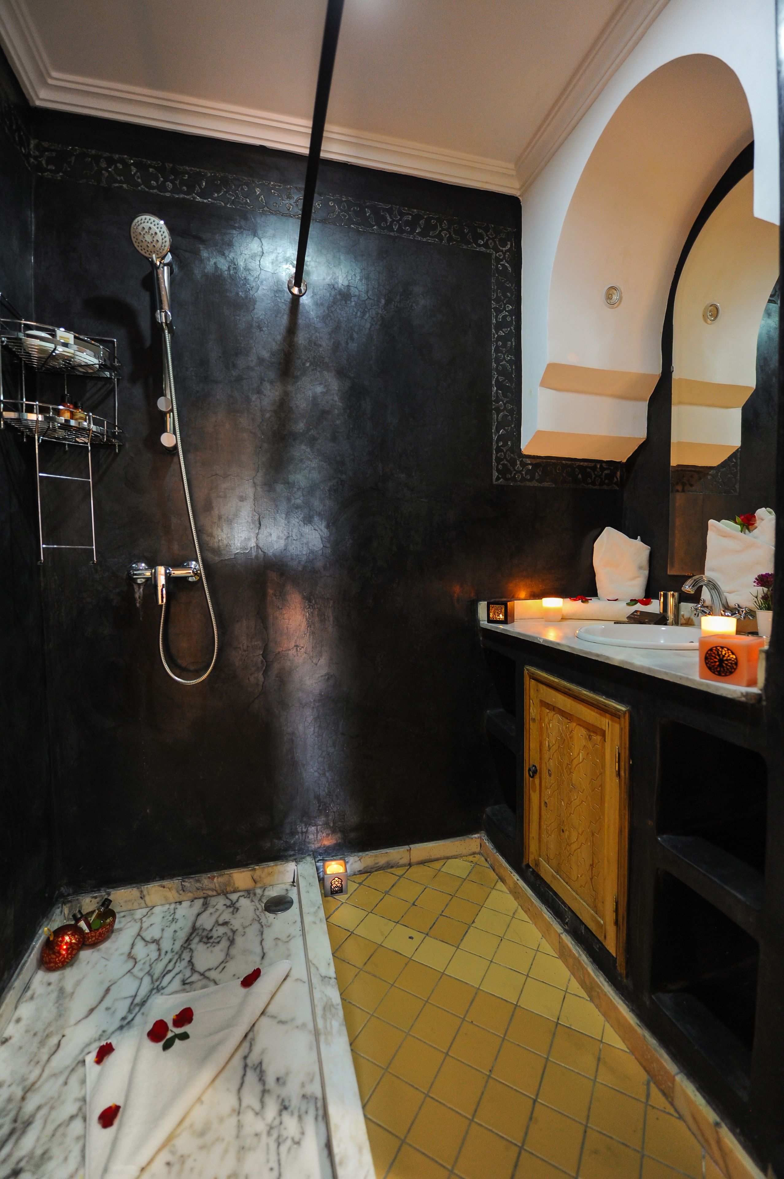 Casa de banho com parede revestida a mosaicos pretos, chuveiro com cabeça de duche manual, lavatório de mármore e armário de madeira.
