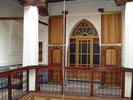 Quarto com porta de madeira, janela com detalhes elaborados e varanda com grade de metal.