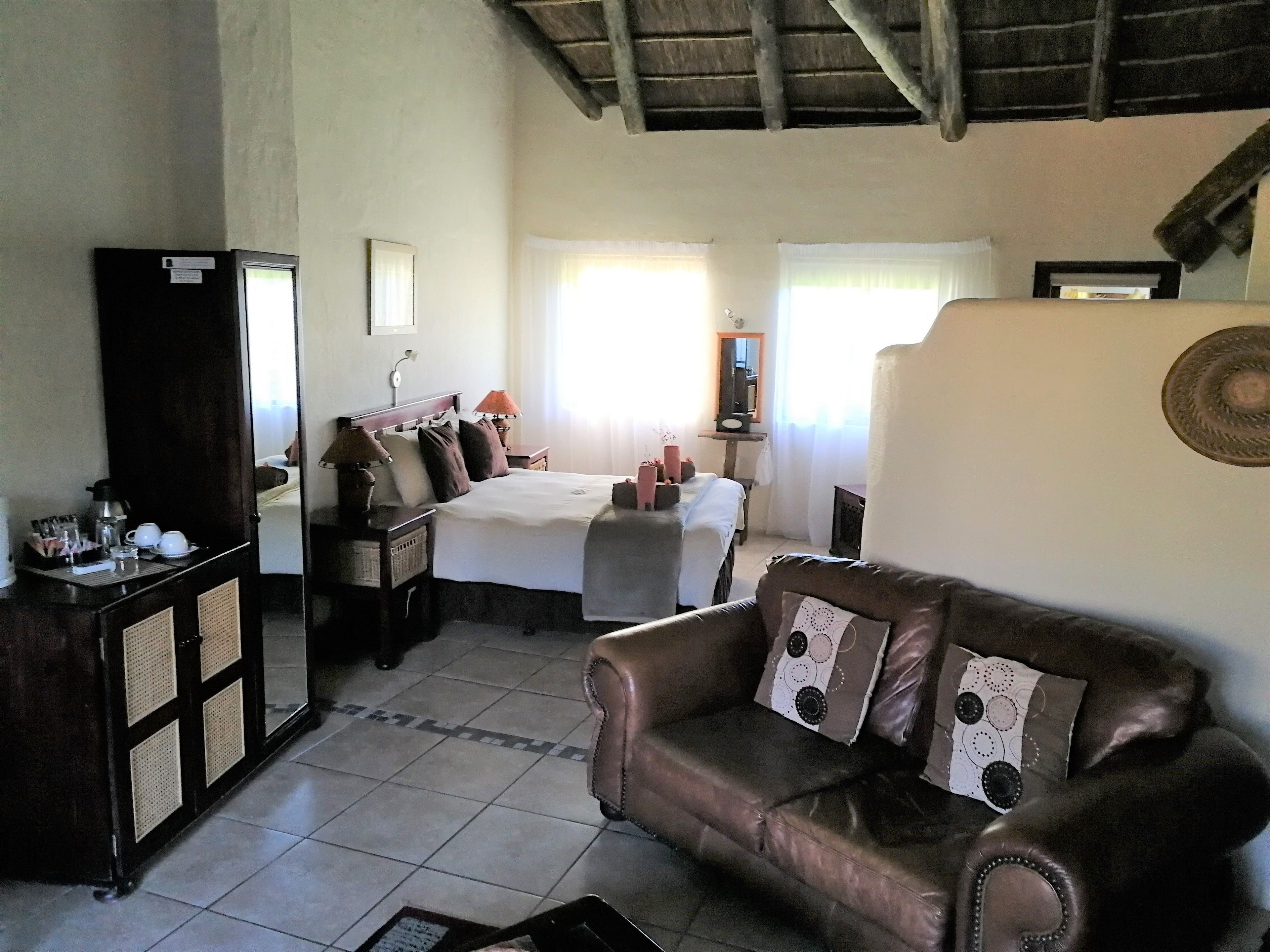 Quarto de hotel com cama, sofá de couro, armário de madeira e escrivaninha com luminária.