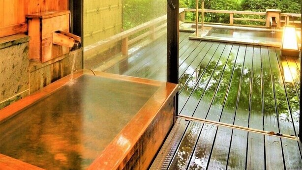 Uma casa de banho japonesa tradicional com um deque de madeira e vista para vegetação exuberante.