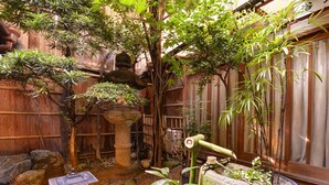 Um jardim japonês tradicional com lanternas de pedra, bambu e diversas plantas em vasos.