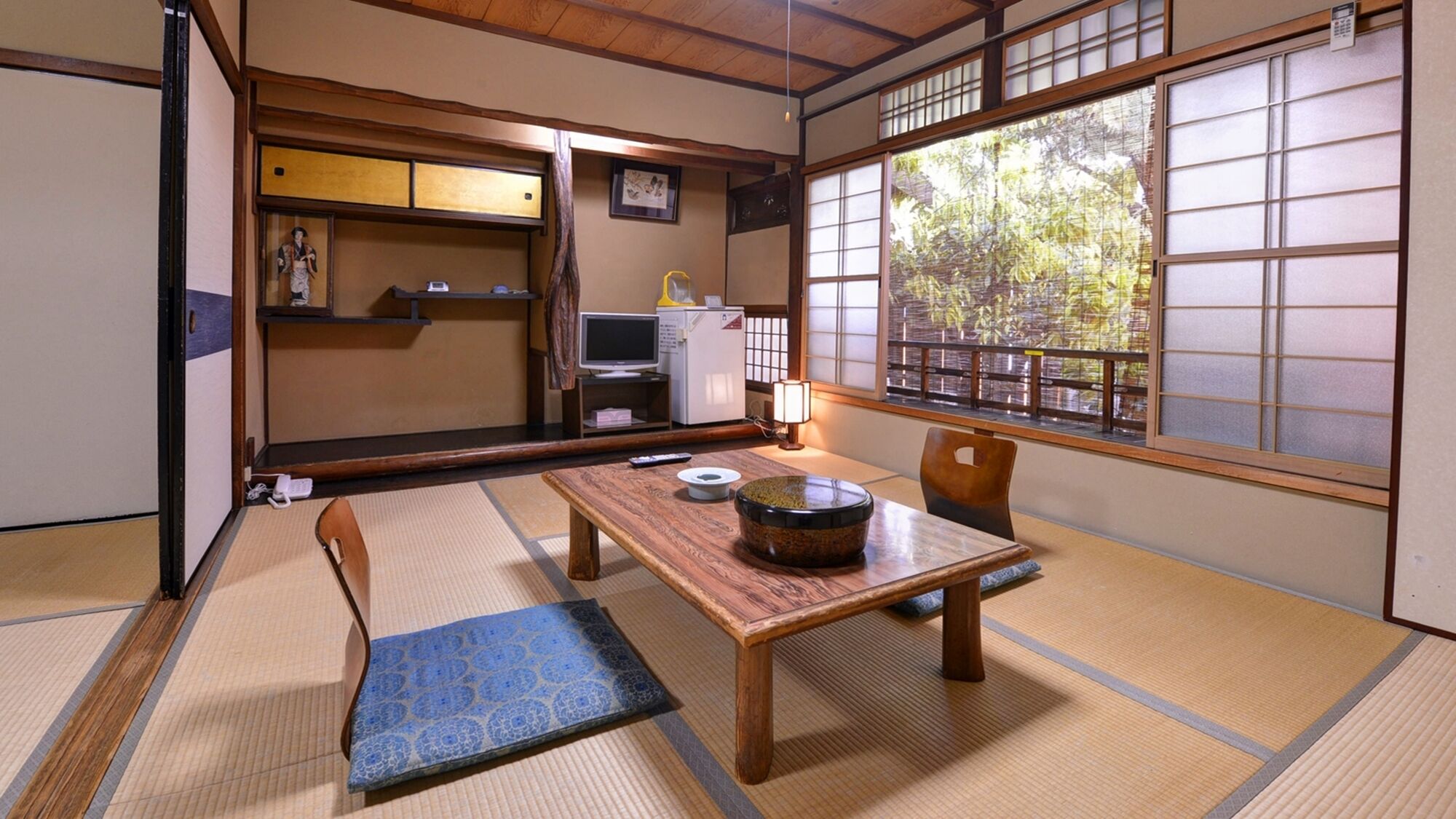 Um quarto japonês tradicional com tatames, uma mesa baixa com uma tigela, uma cadeira, uma TV e um frigorífico.