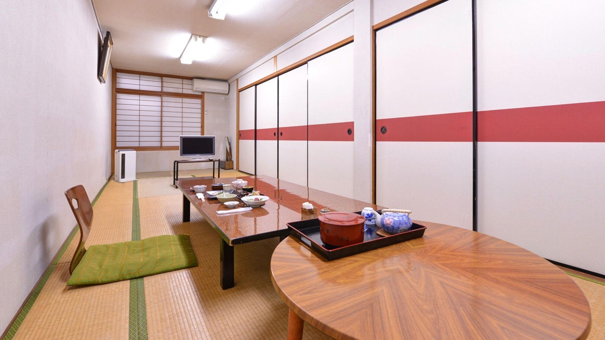 Um quarto japonês tradicional com tatames, uma mesa baixa com pratos, uma televisão e portas deslizantes.