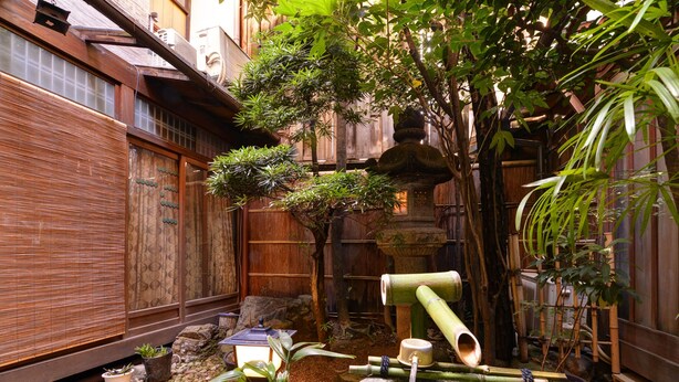 Um jardim japonês tradicional com um reservatório de pedra, bambu e diversas plantas.
