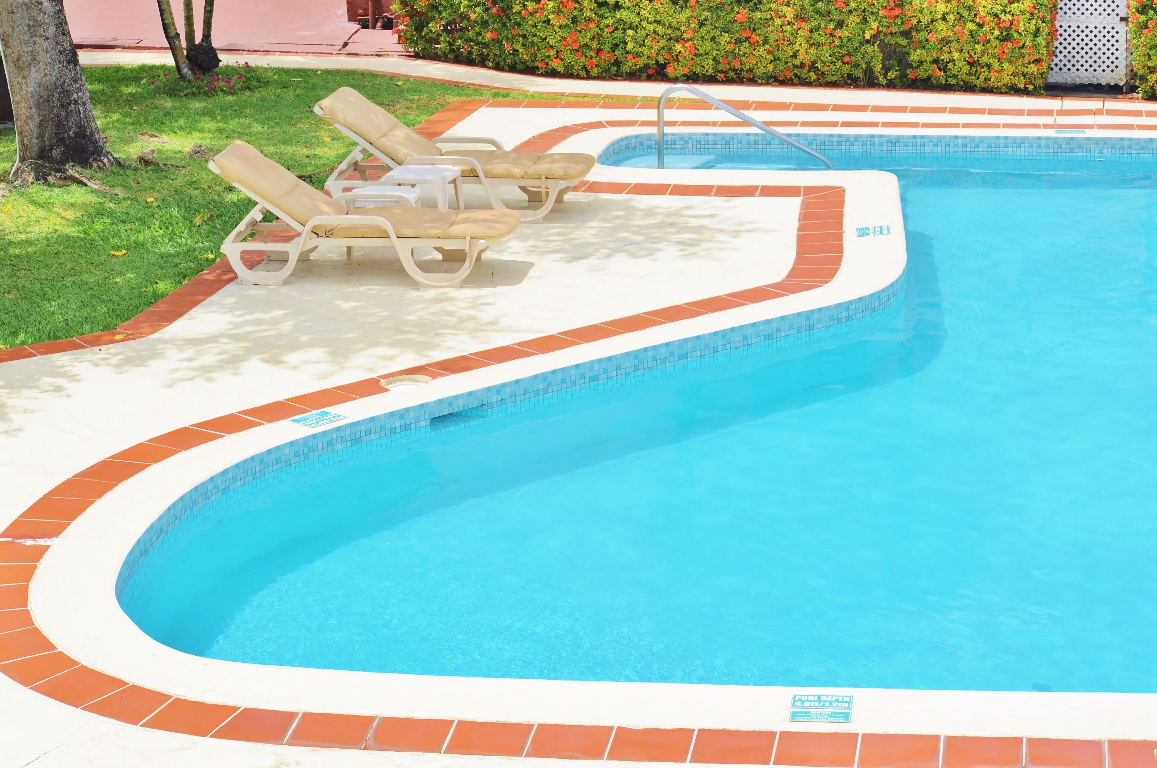 Piscina com borda azulejada, cadeiras de descanso e um revestimento de tijolos.