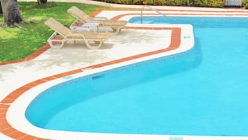 Piscina com borda azulejada, cadeiras de descanso e um revestimento de tijolos.