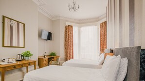 Quarto de hotel com duas camas, uma escrivaninha com cadeira, televisão e um candelabro.