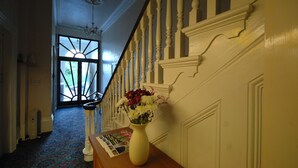 Um corredor com escadaria branca, um candelabro e um vaso com flores sobre uma mesa.