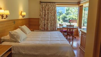 Cama bem arrumada com roupa de cama branca, cabeceira de madeira e duas luminárias fixadas na parede.