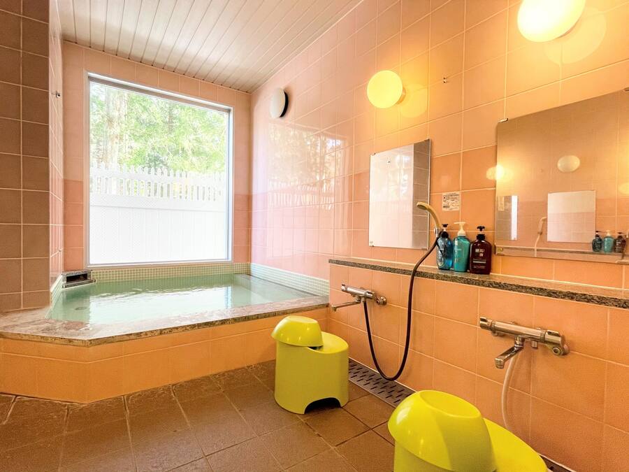 Casa de banho com banheira, latas de lixo amarelas, espelho e janela com vista para árvores.