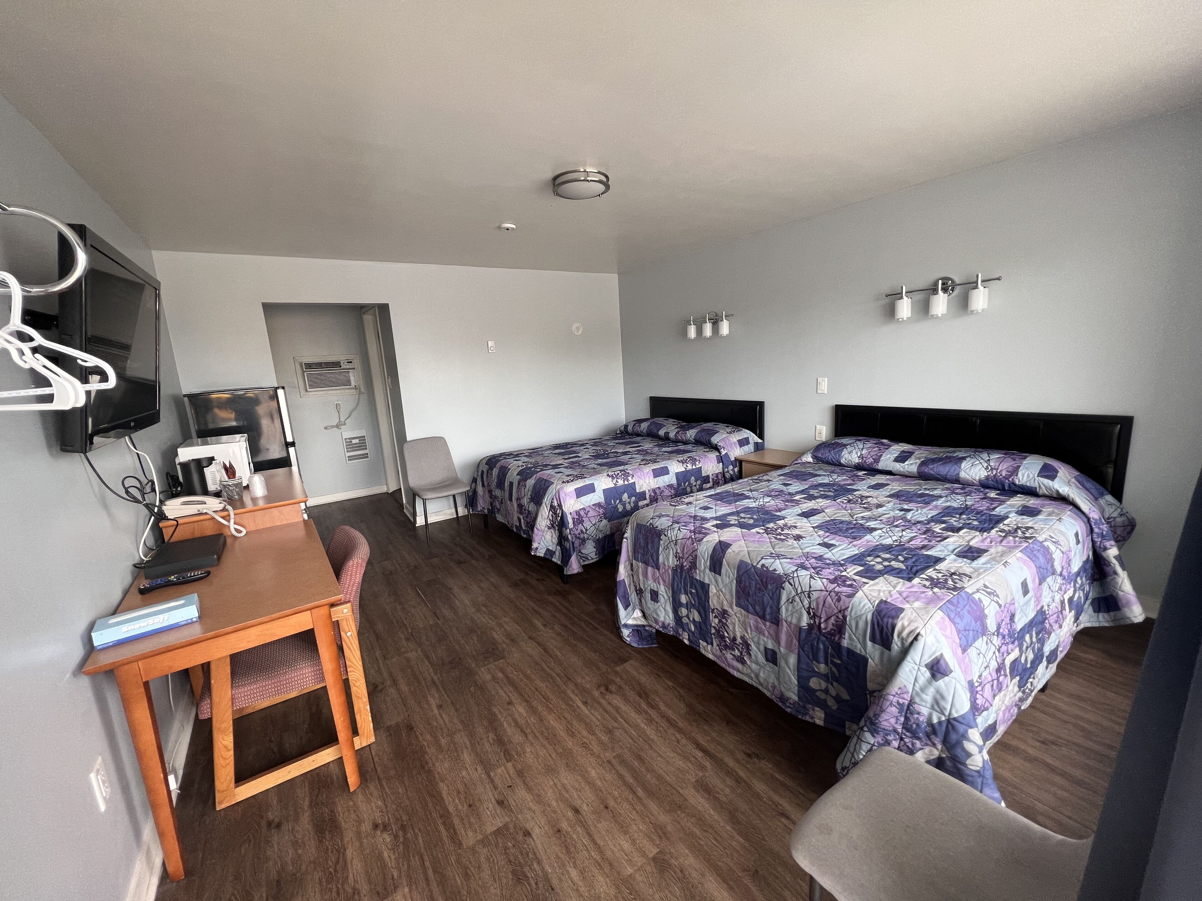 Quarto de hotel com duas camas, uma escrivaninha, uma cadeira, televisão e uma kitchenette.