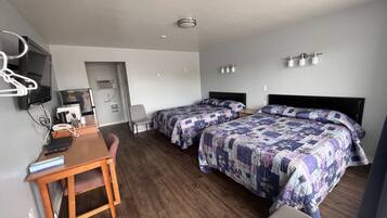 Quarto de hotel com duas camas, uma escrivaninha, uma cadeira, televisão e uma kitchenette.
