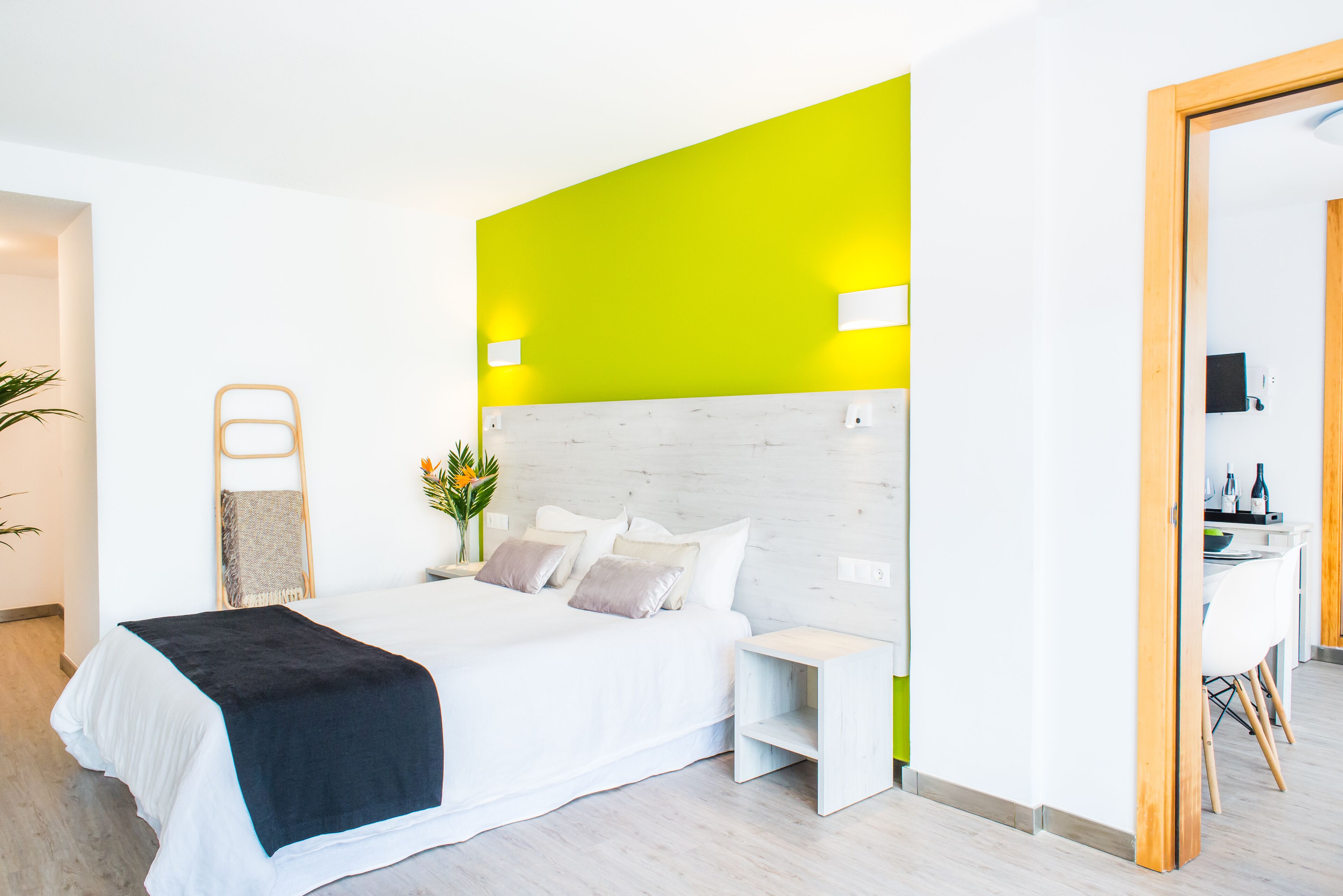 Quarto de hotel moderno com uma cama, mesas de cabeceira, uma escrivaninha e uma parede de destaque verde vibrante.
