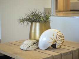 Mesa de madeira com concha decorativa e um vaso dourado com plantas verdes.
