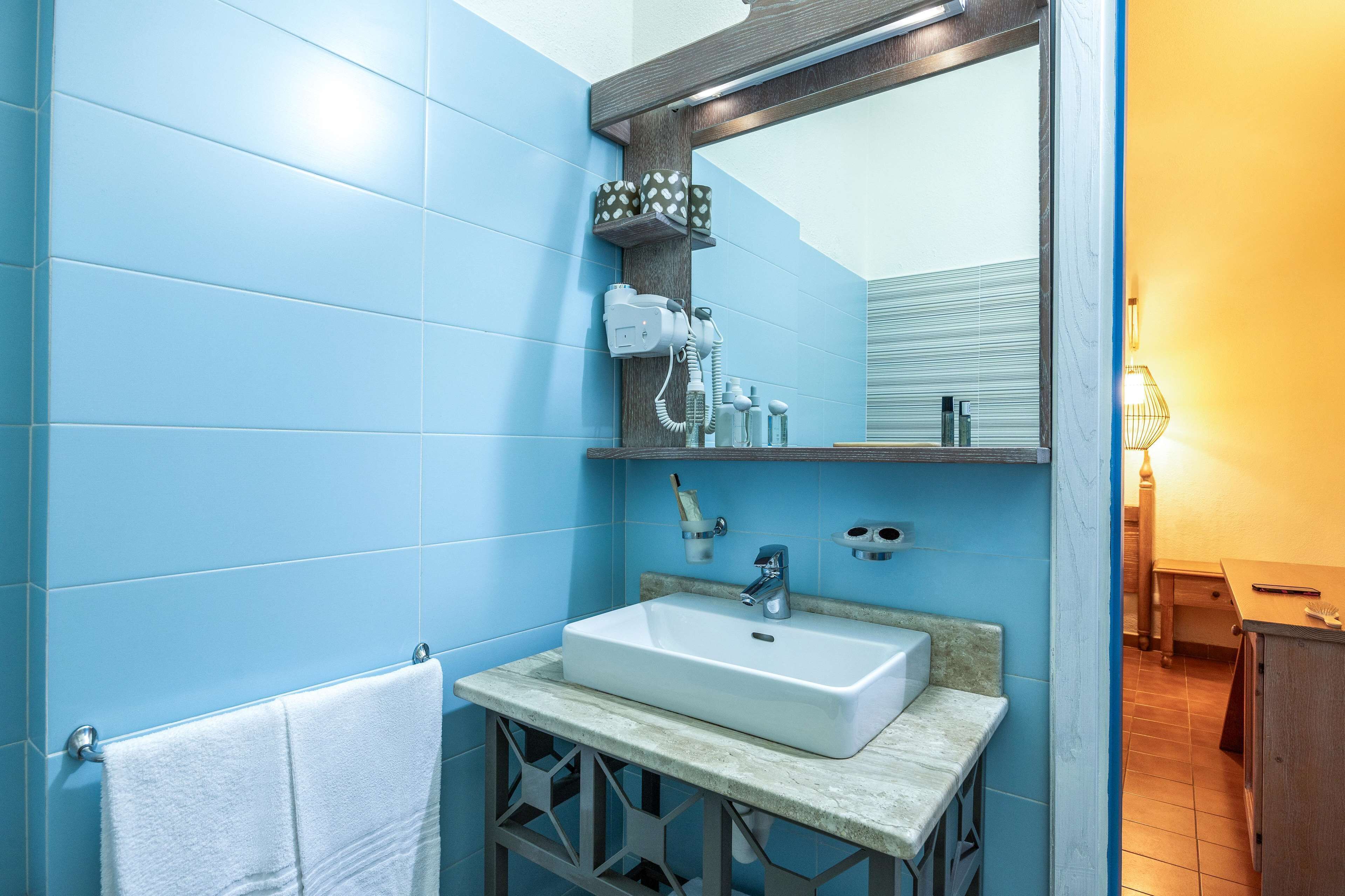 Casa de banho com uma pia branca, azulejos azuis e toucador de madeira.