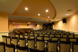 Uma sala de conferências com fileiras de cadeiras, um palco e um banner com a inscrição 'LYRA'.