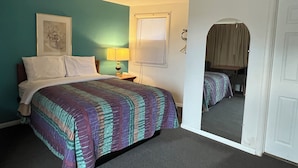 Quarto de hotel com uma cama, abajur, quadro pendurado na parede e um espelho refletindo o ambiente.