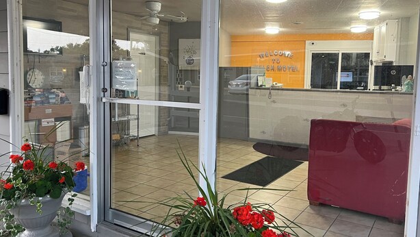 Uma área de recepção de hotel com porta de vidro, um relógio e um letreiro de boas-vindas.