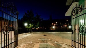 Um pátio pavimentado com um emblema circular, portões de metal e um edifício ao fundo.
