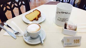 Uma mesa com uma fatia de bolo, uma xícara de café, uma caneca e uma caixa com a etiqueta 'SAN BERARDO'.