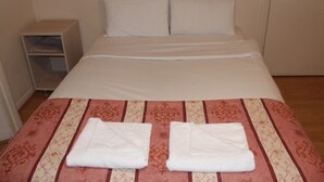 Cama bem arrumada com lençóis brancos e duas toalhas dobradas sobre um cobreleito estampado.