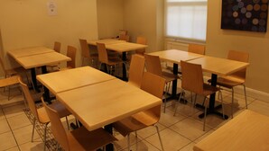 Uma sala de aula com várias mesas e cadeiras de madeira, um relógio na parede e uma janela com persianas.