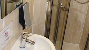 Uma casa de banho com uma pia branca, um espelho e cabine de duche em vidro.
