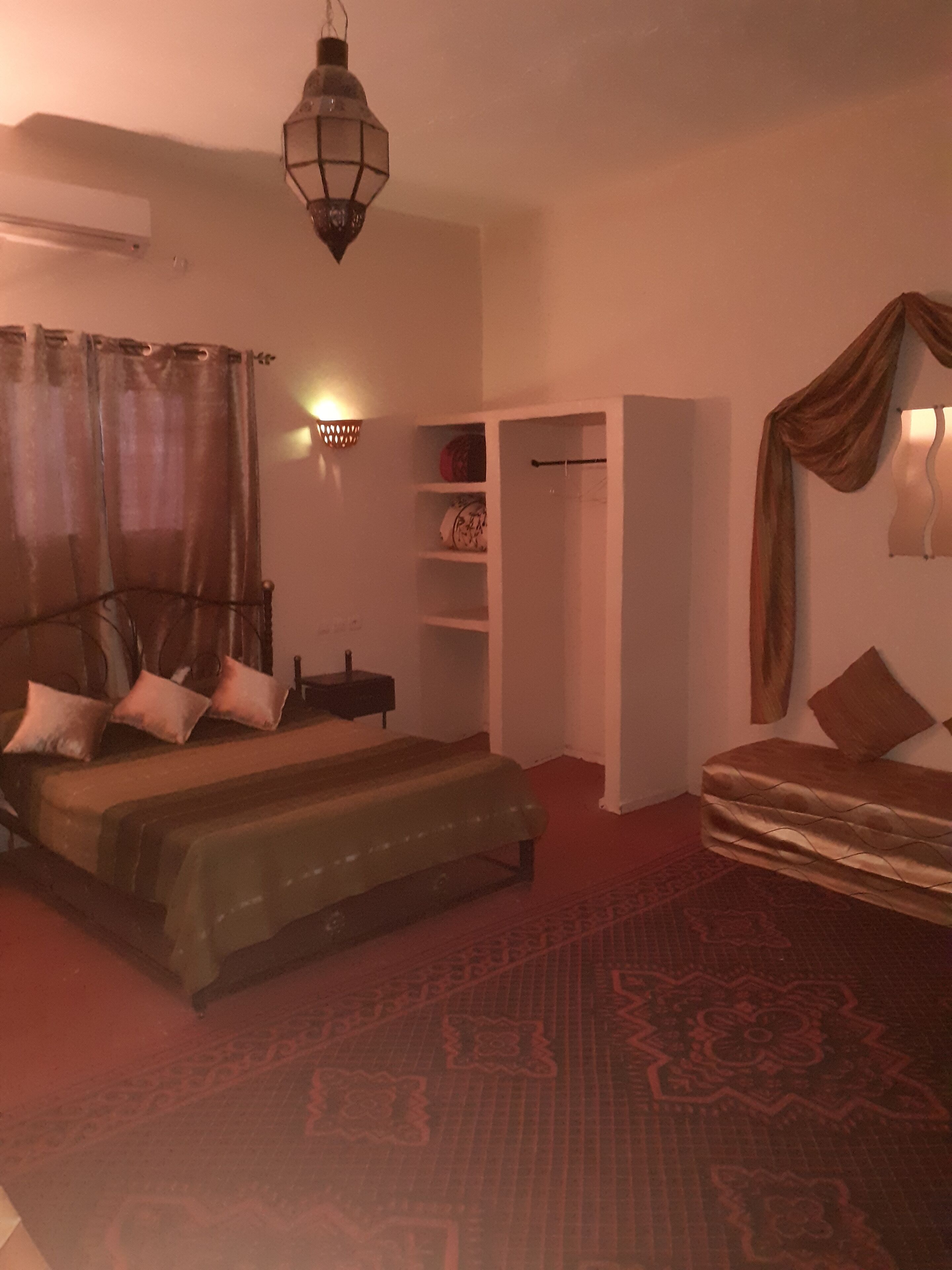 Quarto com cama, mesa de cabeceira, guarda-roupa, luminária pendente e tapete estampado.