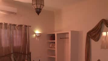 Quarto com cama, mesa de cabeceira, guarda-roupa, luminária pendente e tapete estampado.