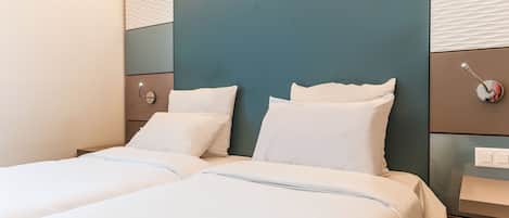 Quarto de hotel com duas camas, uma parede de destaque cor turquesa e uma mesa de cabeceira com abajur.