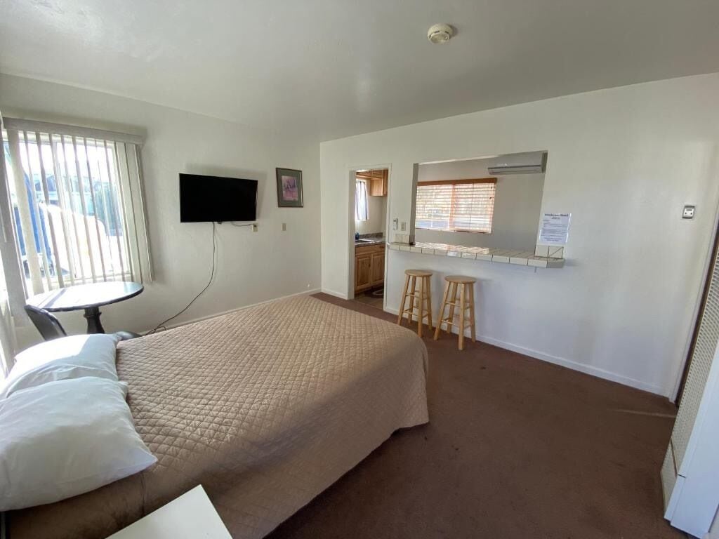 Um quarto com uma cama, televisão, escrivaninha e janelas.