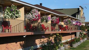 Hotel com área de estar externa coberta, cadeiras vermelhas e cestos de flores pendurados.