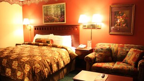Quarto de hotel com uma cama grande, um sofá, uma mesinha de cabeceira e duas luminárias fixadas na parede.