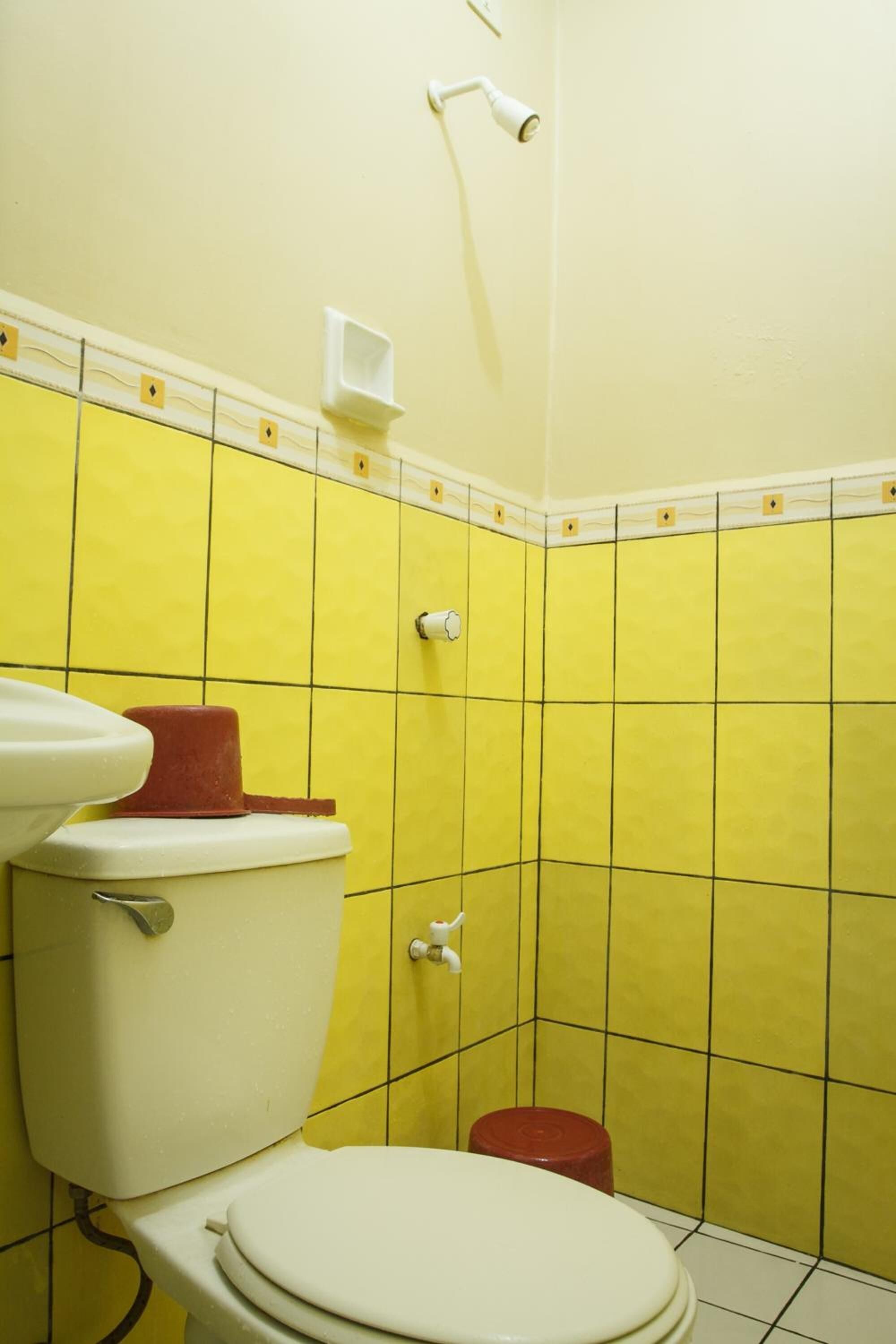 Um banheiro com paredes azulejadas amarelas, vaso sanitário branco e lixeira vermelha.