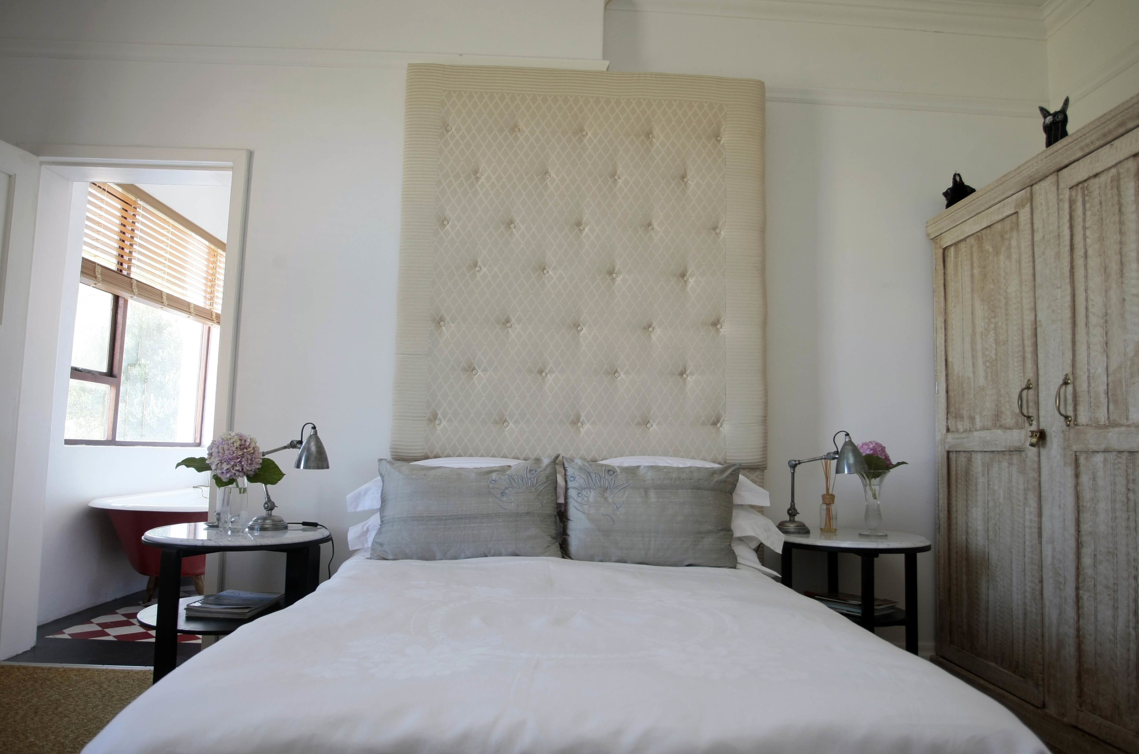 Um quarto com uma cama grande, um guarda-roupa de madeira, uma mesinha com abajur e uma janela com persianas.