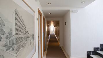 Corredor de hotel com um longo hall, portas à esquerda e escada à direita.