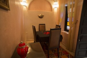 Uma sala de jantar com uma mesa posta para dois, um objeto decorativo vermelho sobre a mesa e uma janela com cortinas.
