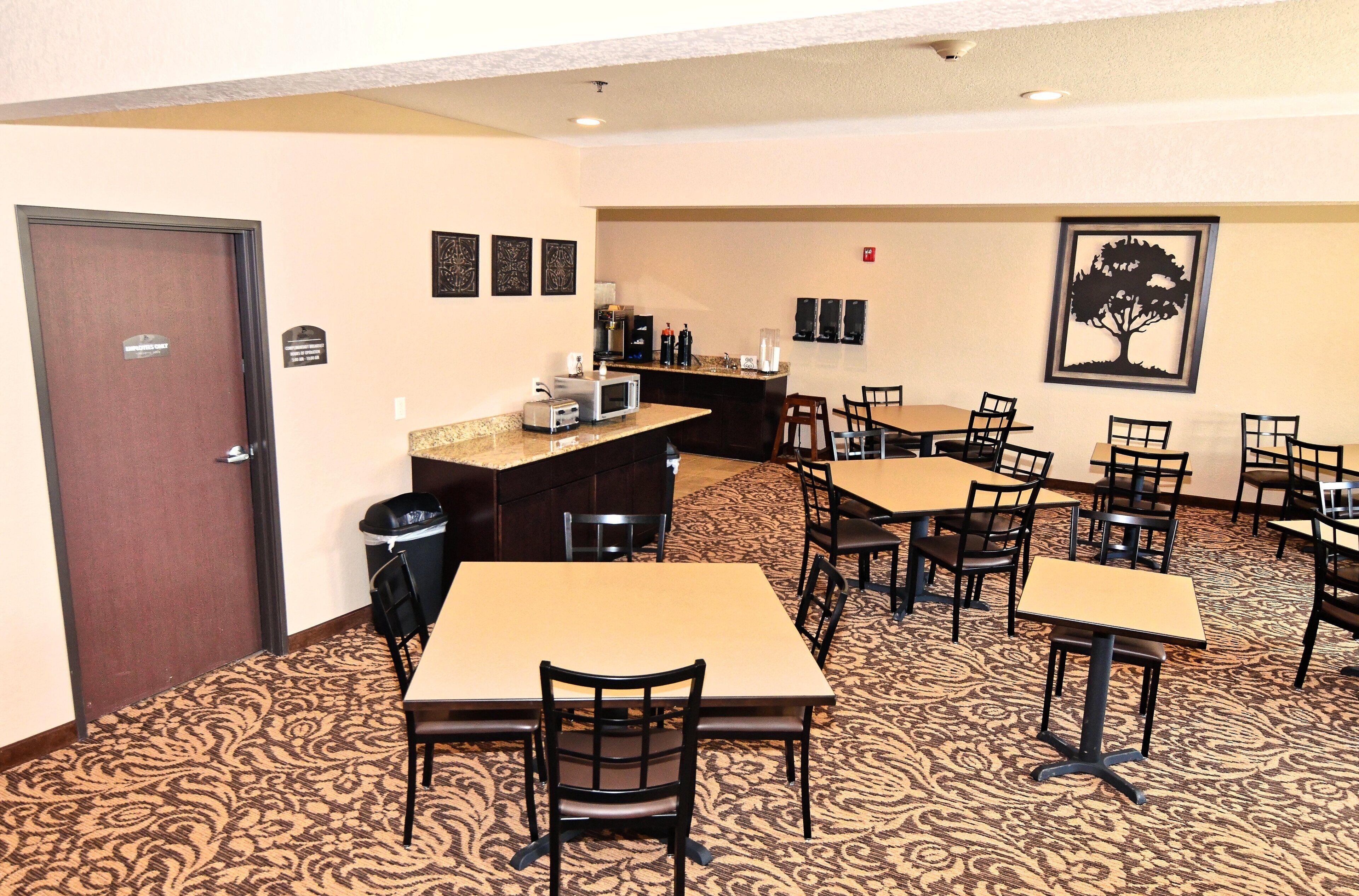 Uma sala de jantar de hotel com várias mesas e cadeiras, um espaço para café e um tapete estampado.