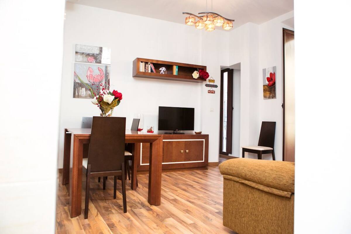Uma sala de estar moderna com uma mesa de jantar de madeira, um sofá, uma televisão e uma estante de livros.