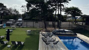 Um quintal com um deck de madeira, uma piscina e móveis de exterior.